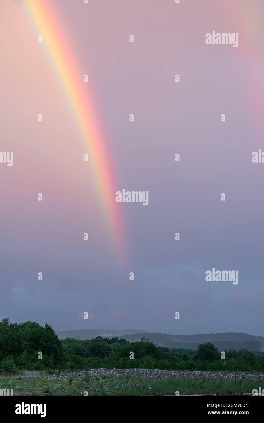 A large rainbow in the blue-pink sky over the mountains and forest ...