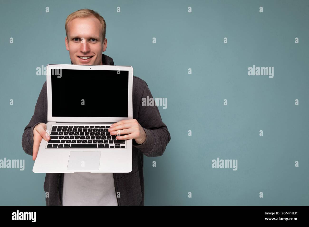 Close-up portrait of handsome smiling blonde man holding computer ...