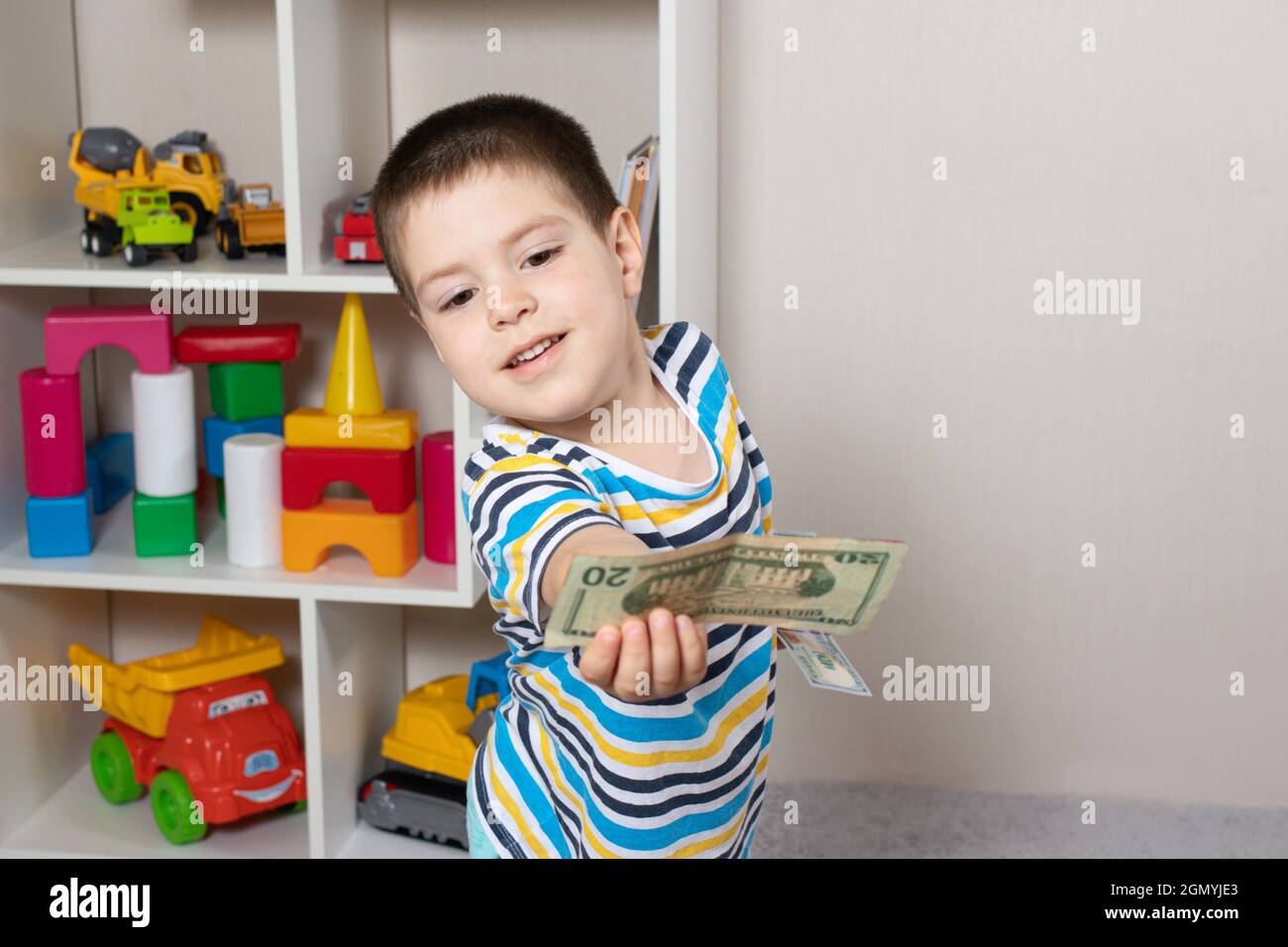 A young child boy of 4 years stretches out his hand with dollar bills ...