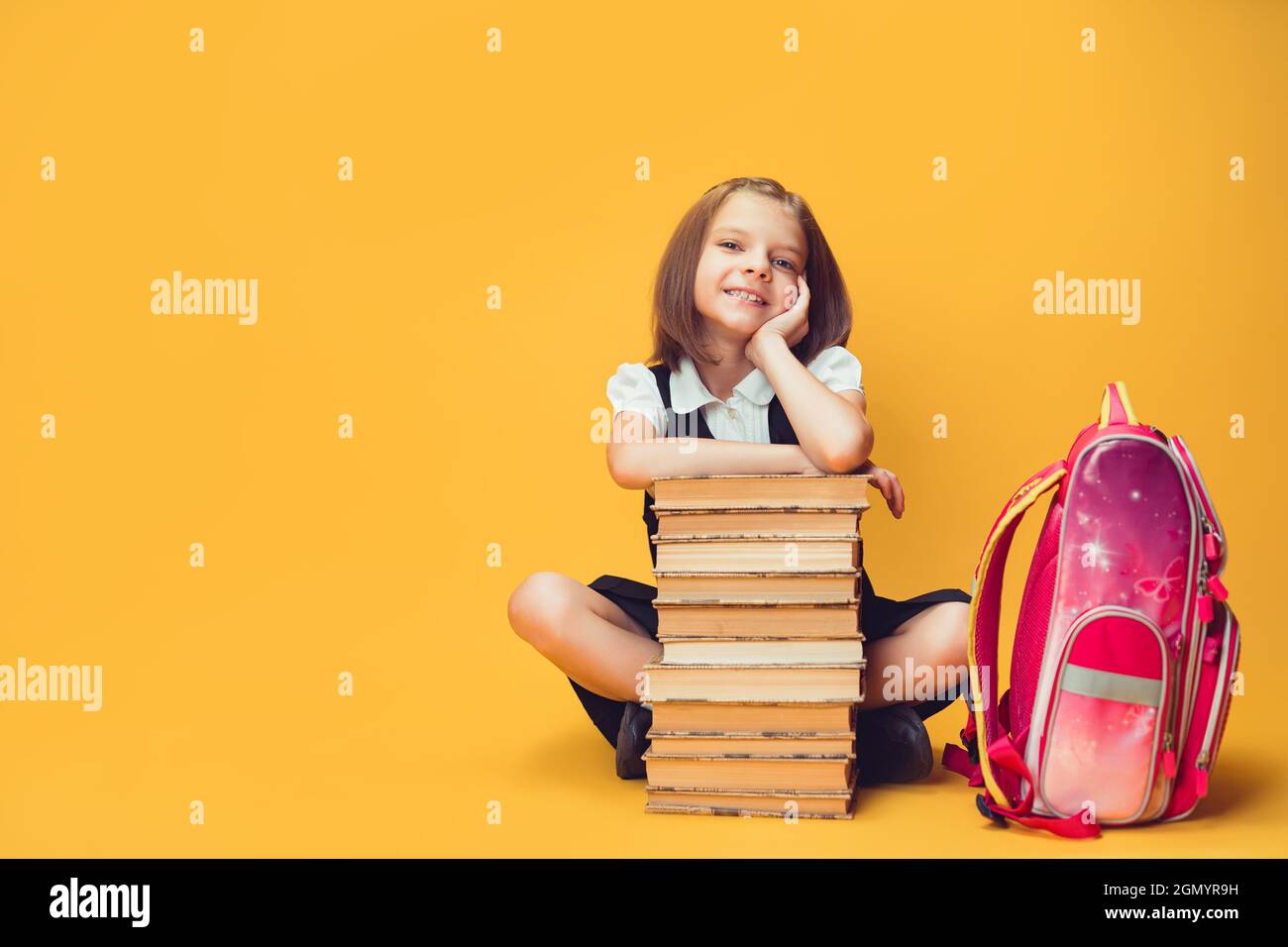Smiling pupil sitting behind a stack of books with backpack. Concept of ...