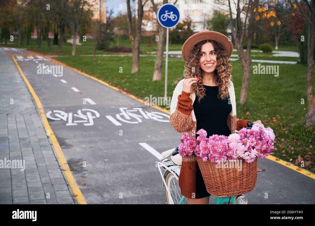 Curly woman riding vintage bicycle with big basket of pink flowers ...