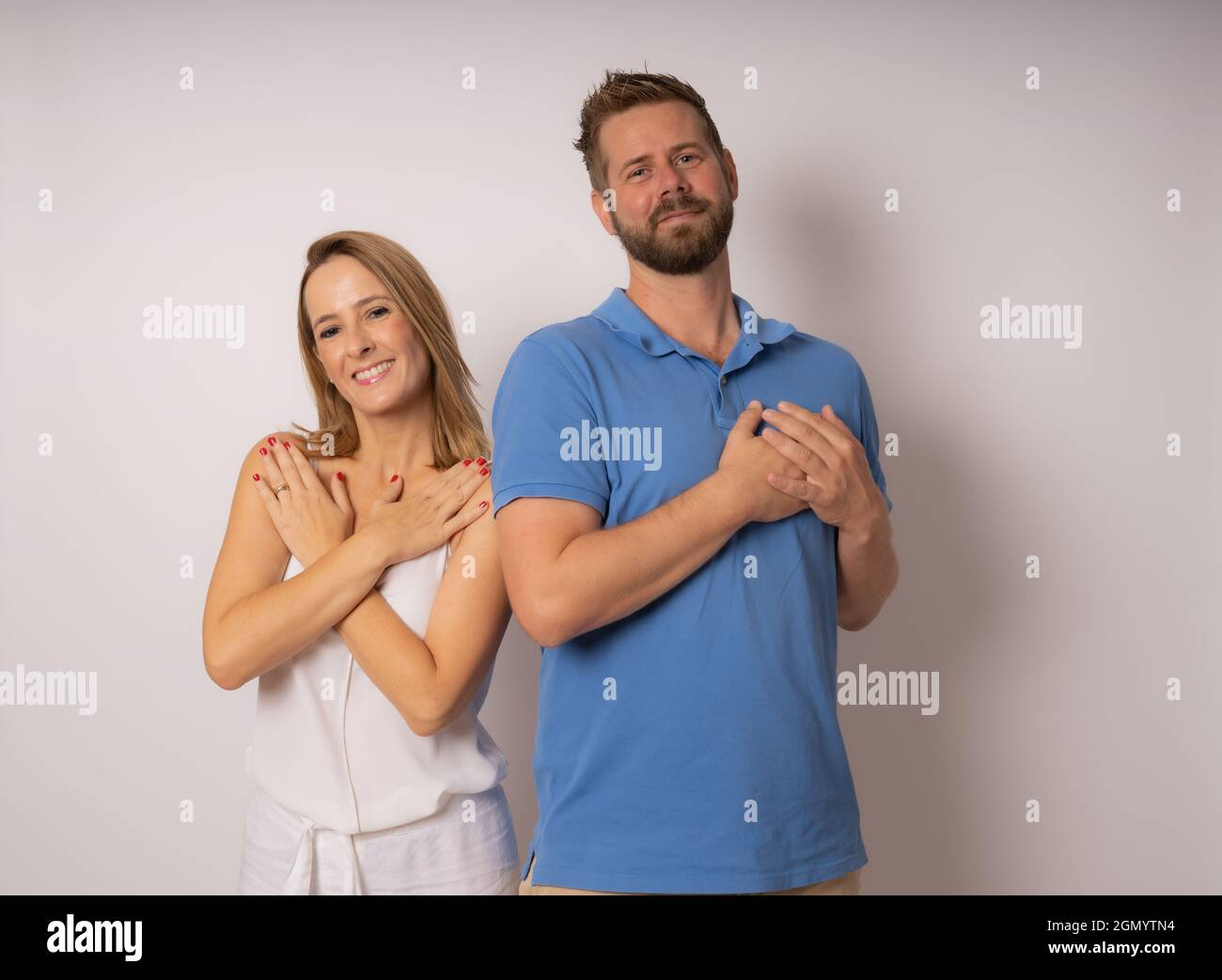Grateful millennial couple looking at camera holding hands on chest ...