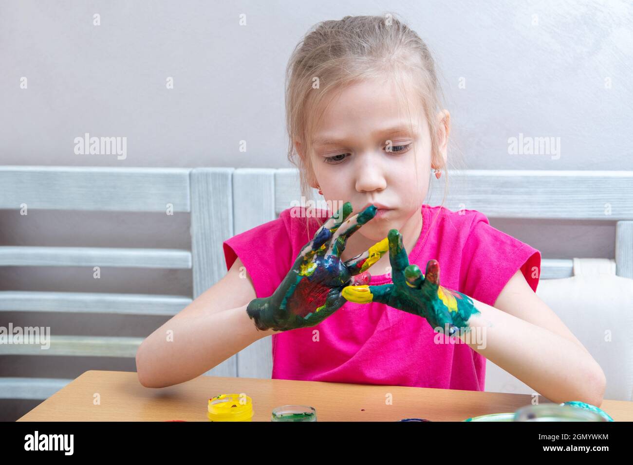Little girl with colorful painted hands. A concentrated girl smears ...