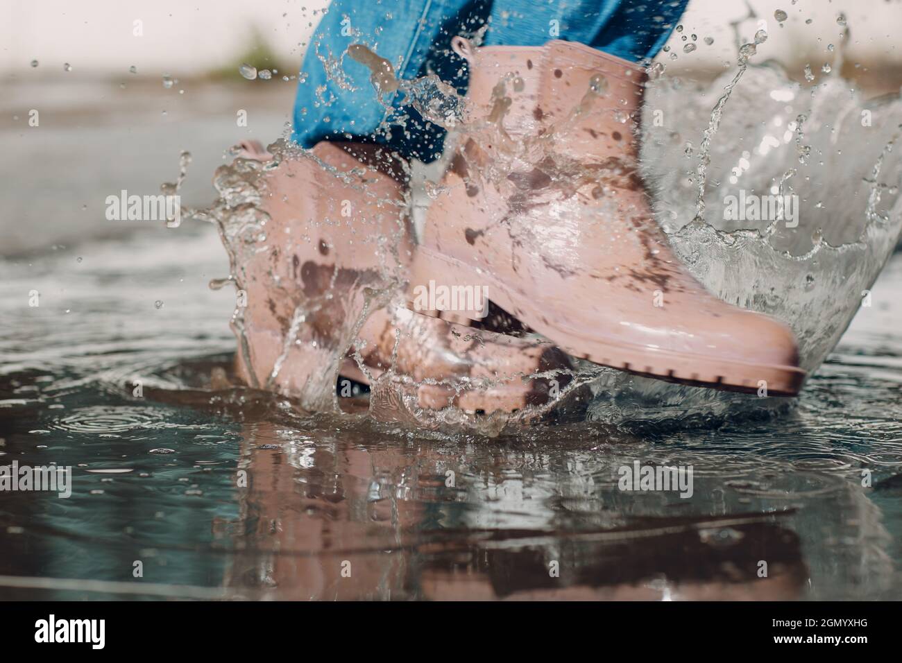 Woman wearing rain rubber boots walking running and jumping into puddle with water splash and ...