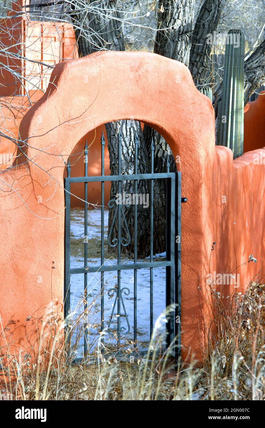 Adobe wall surrounds back yard. Arched entry is guarded by a black iron ...