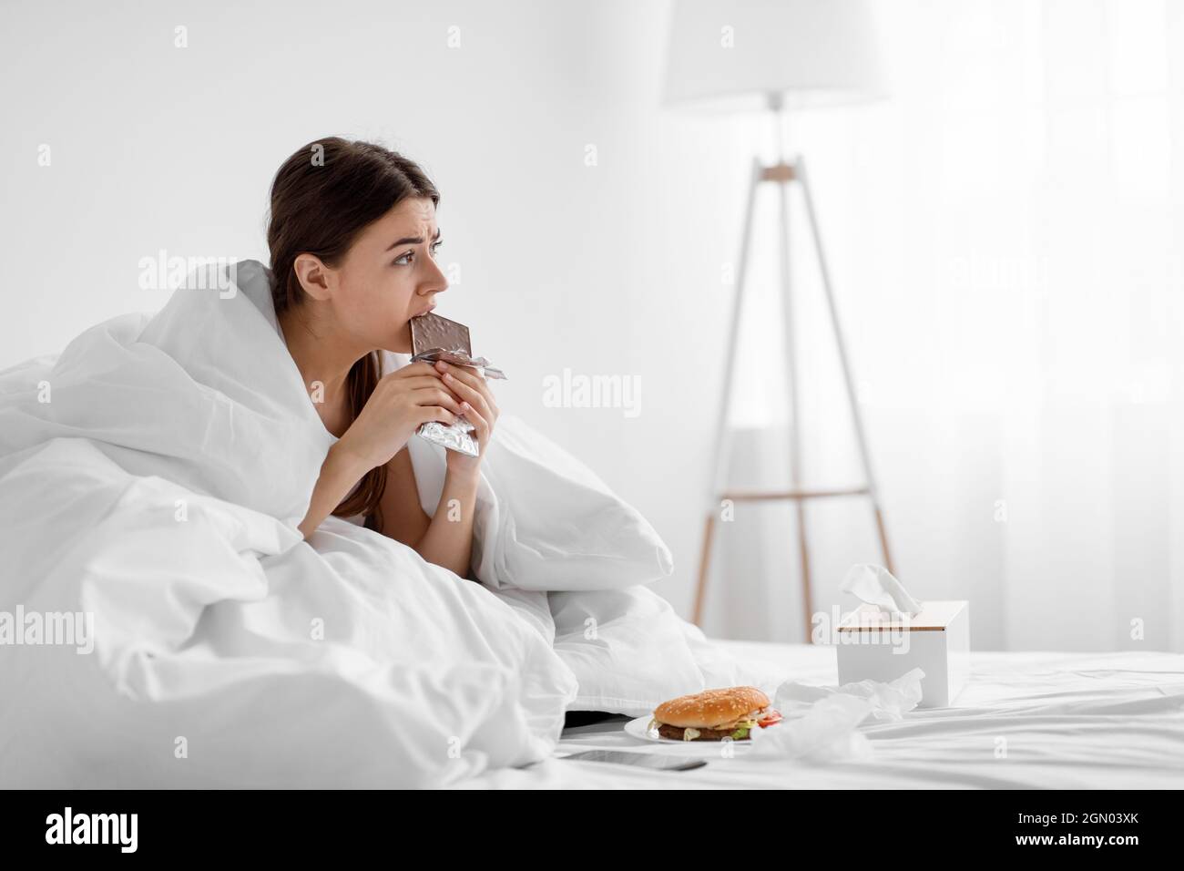 Disappointed upset millennial woman eating chocolate bar on bed with ...