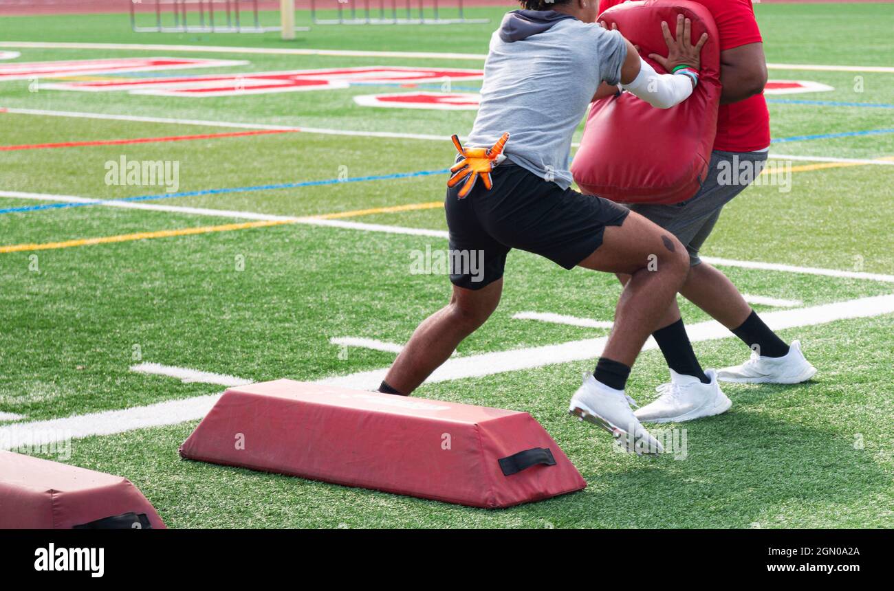 A high school football player hits the pad his coach is holding after ...