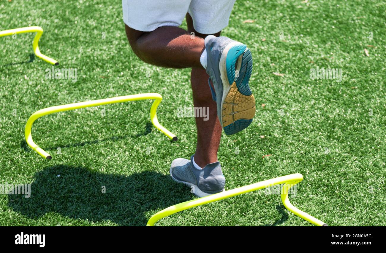 The lower legs of a runner rnning drills over yellow six inch mini hurdles on a turf field Stock ...