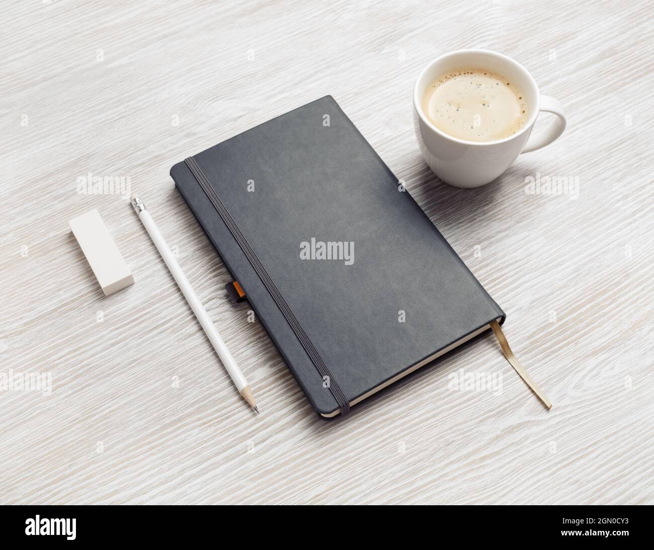 Blank closed notebook, pencil, eraser and coffee cup on light wood ...