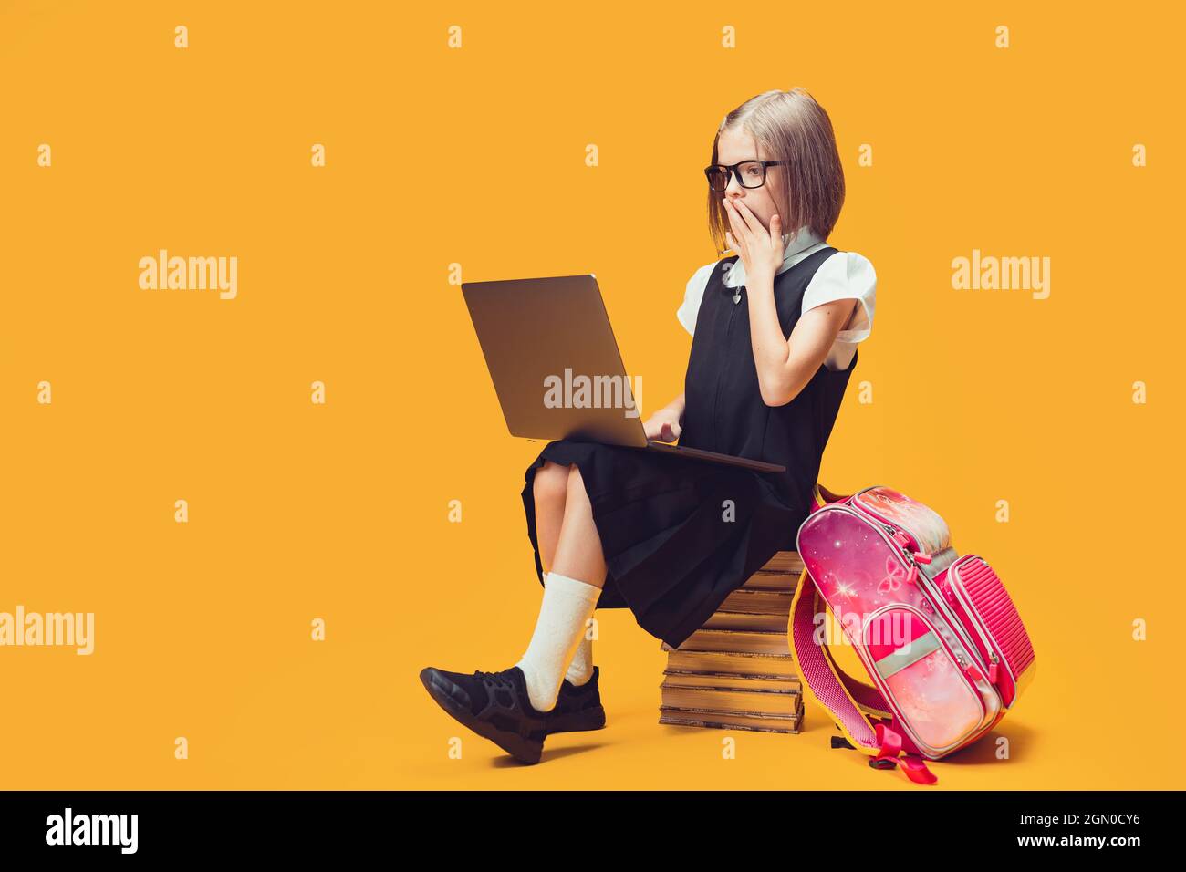 Full length pupil in shock sitting on the stack of books looking at ...