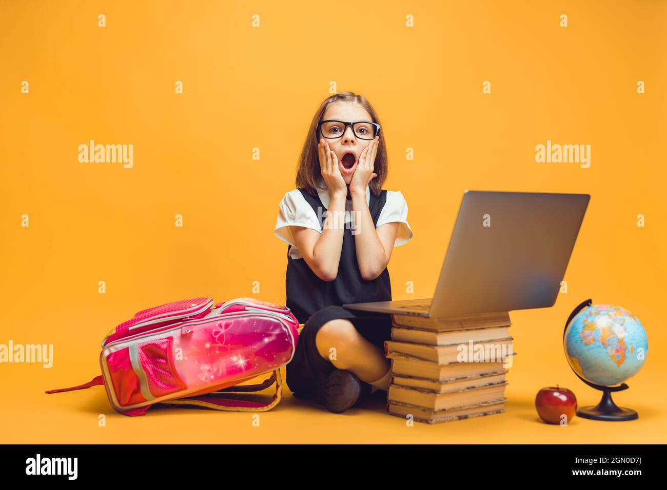 Full length shocked schoolgirl sit behind a stack of books with pc Look ...