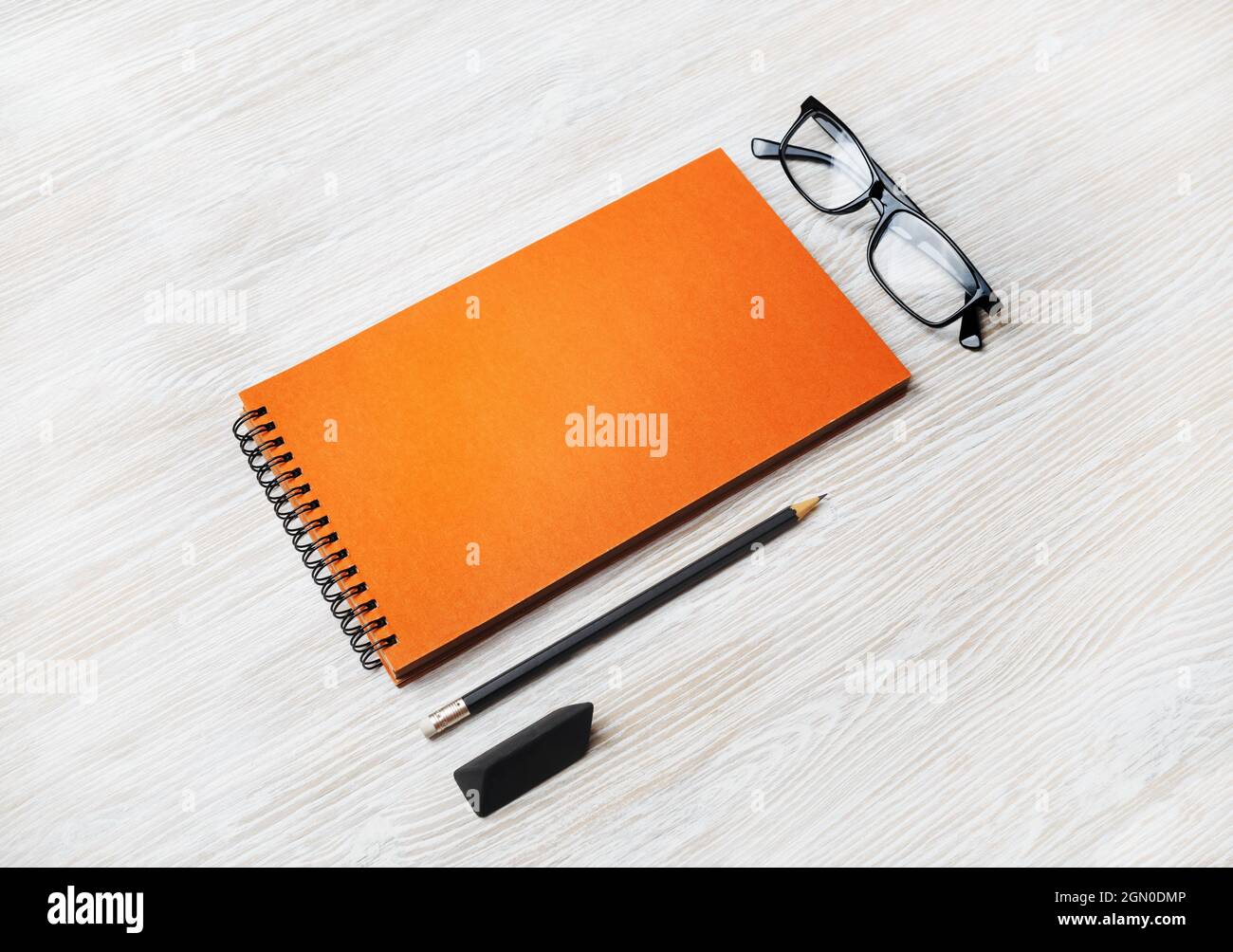 Blank orange notepad, glasses, pencil and eraser on light wooden ...