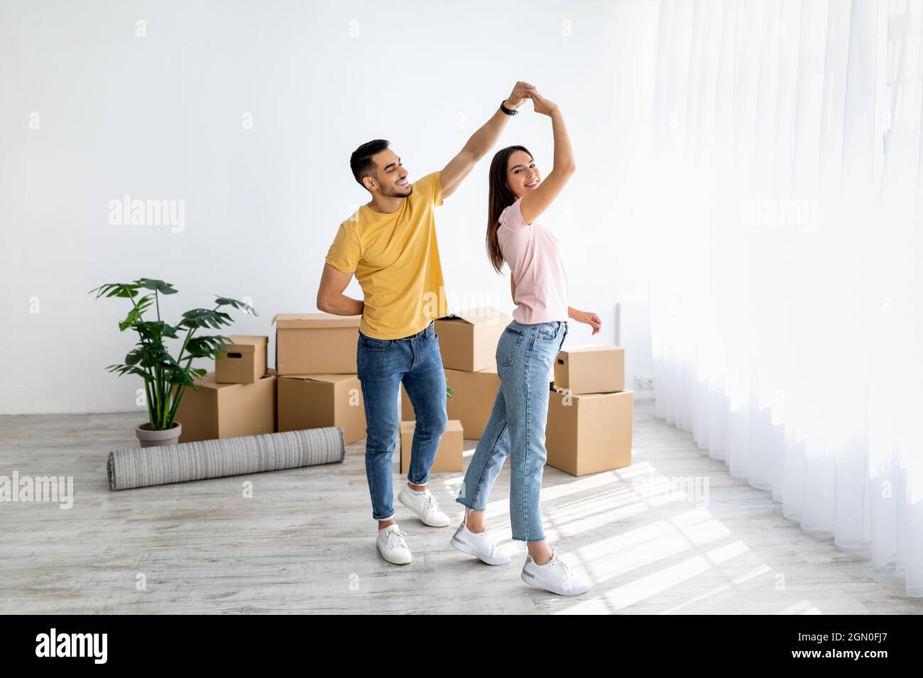 Affectionate multiracial couple dancing in their house among carton ...