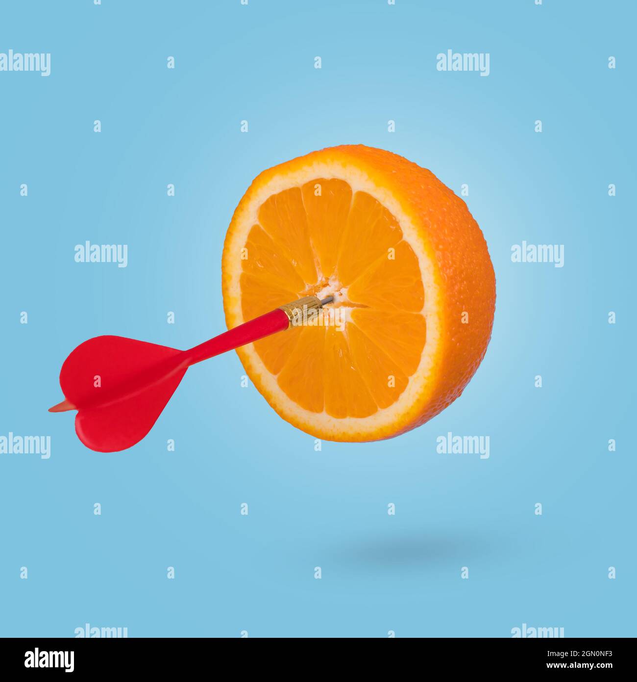 Orange fruit slice with circular target marked and red dart on a blue ...
