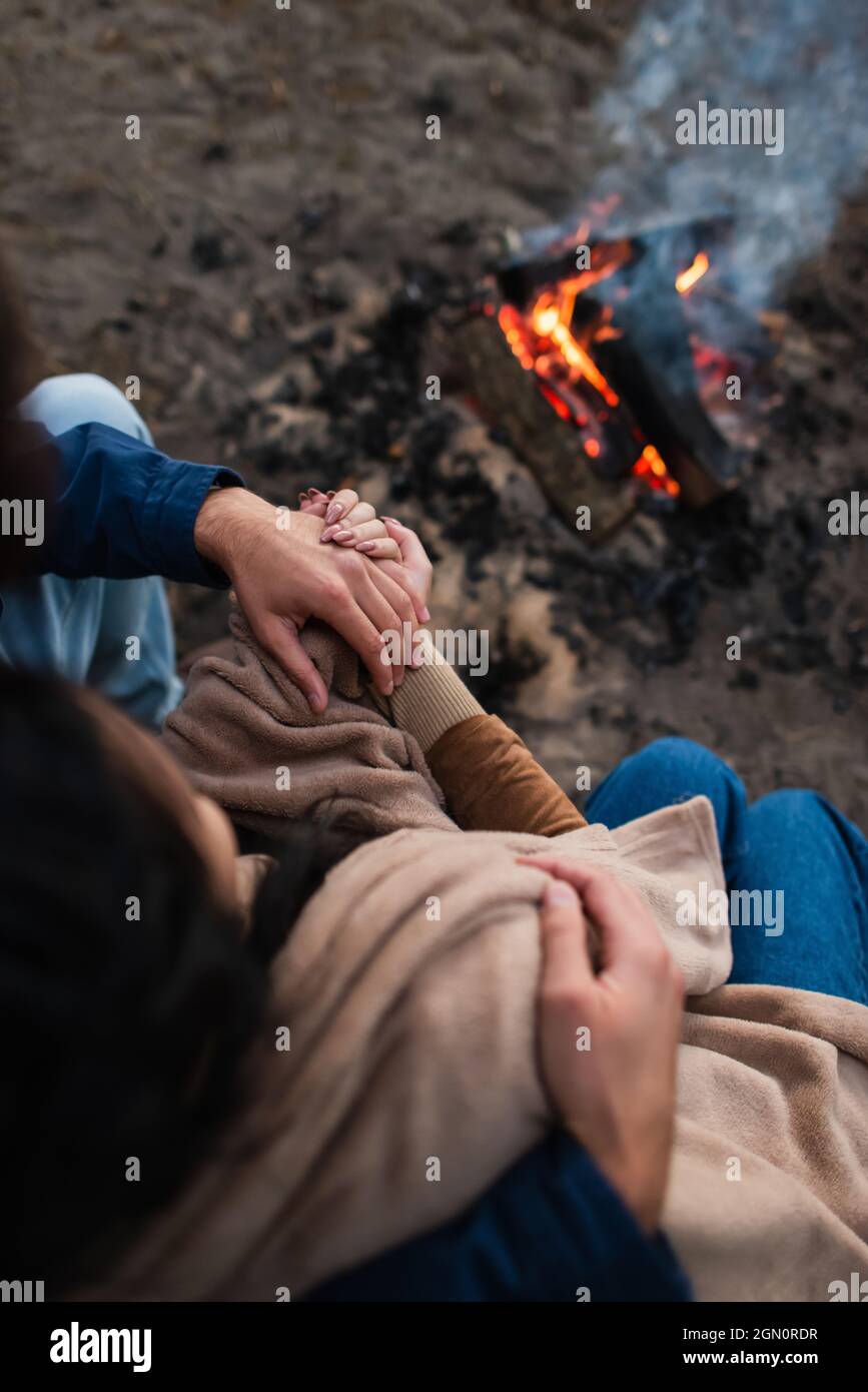 Overhead view of couple holding hands while warming near campfire Stock ...