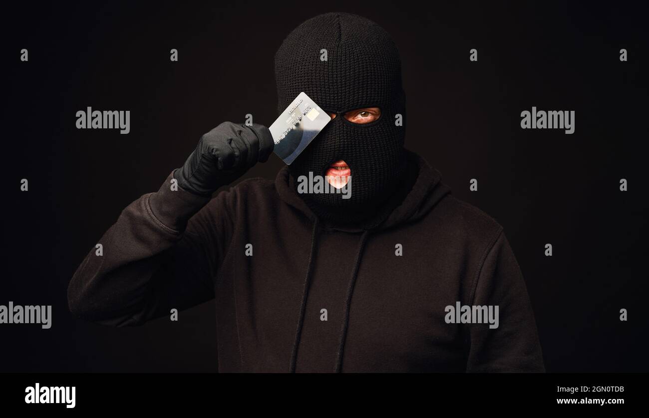 Thief in black balaclava holding black credit card. Banking and non ...
