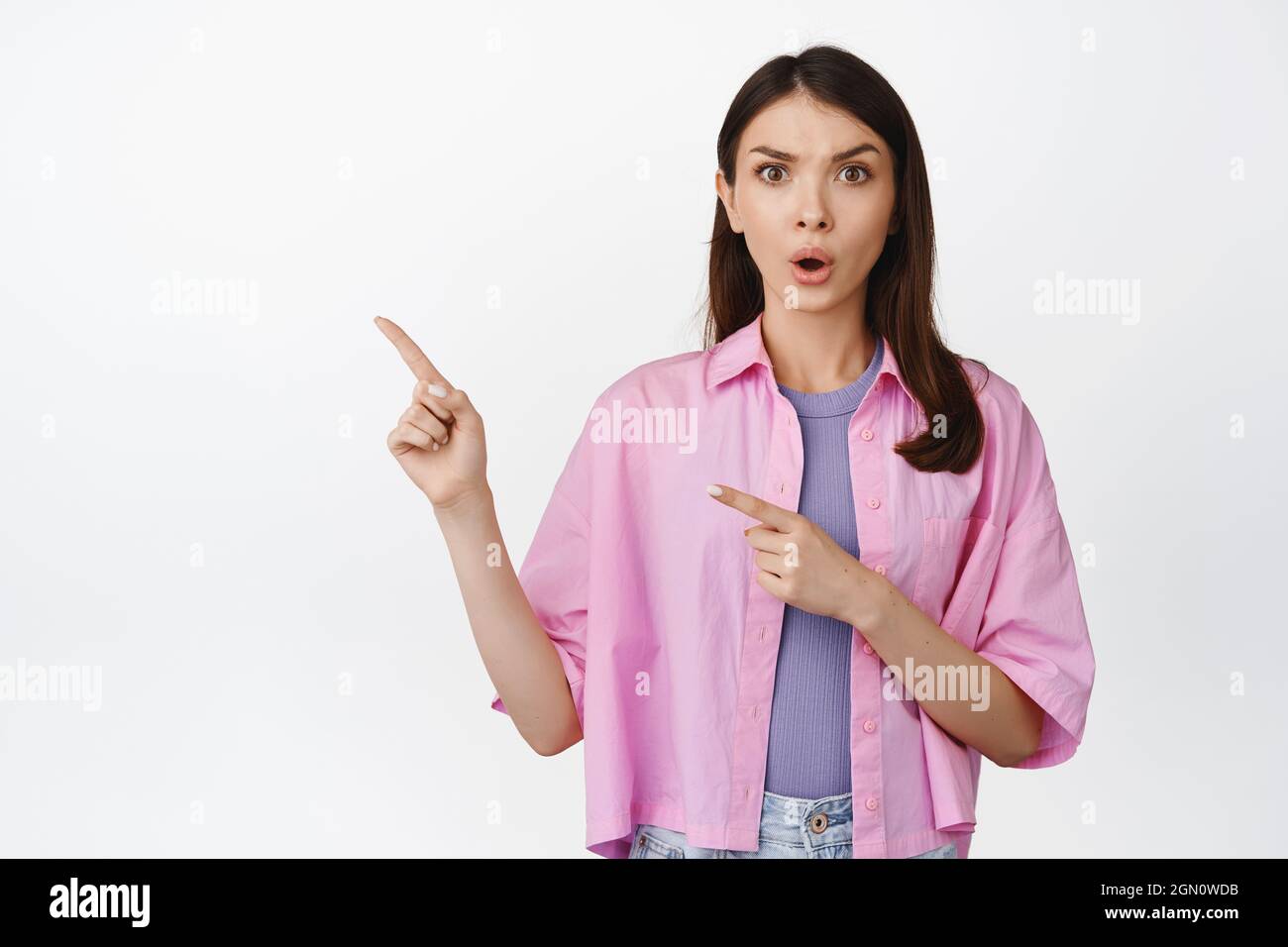 Shocked and confused woman pointing at upper left corner, staring ...