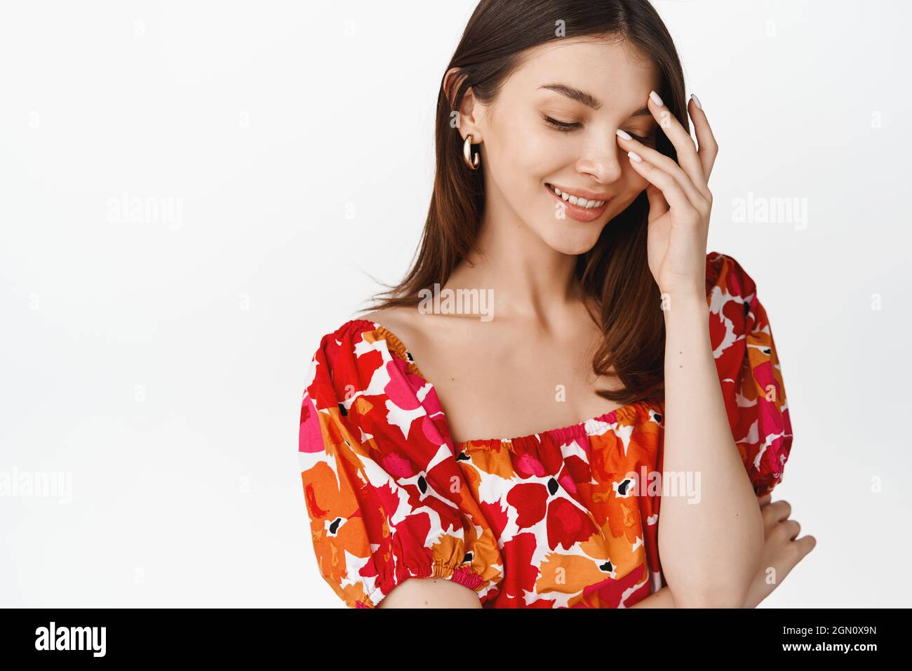 Beautiful young woman smiling coquettish, touching her face and looking ...