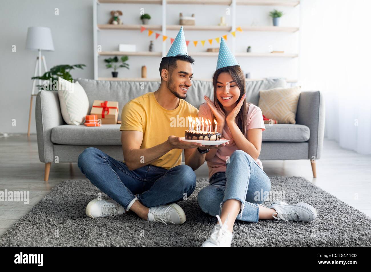 Happy millennial couple wearing party hats, celebrating birthday with ...