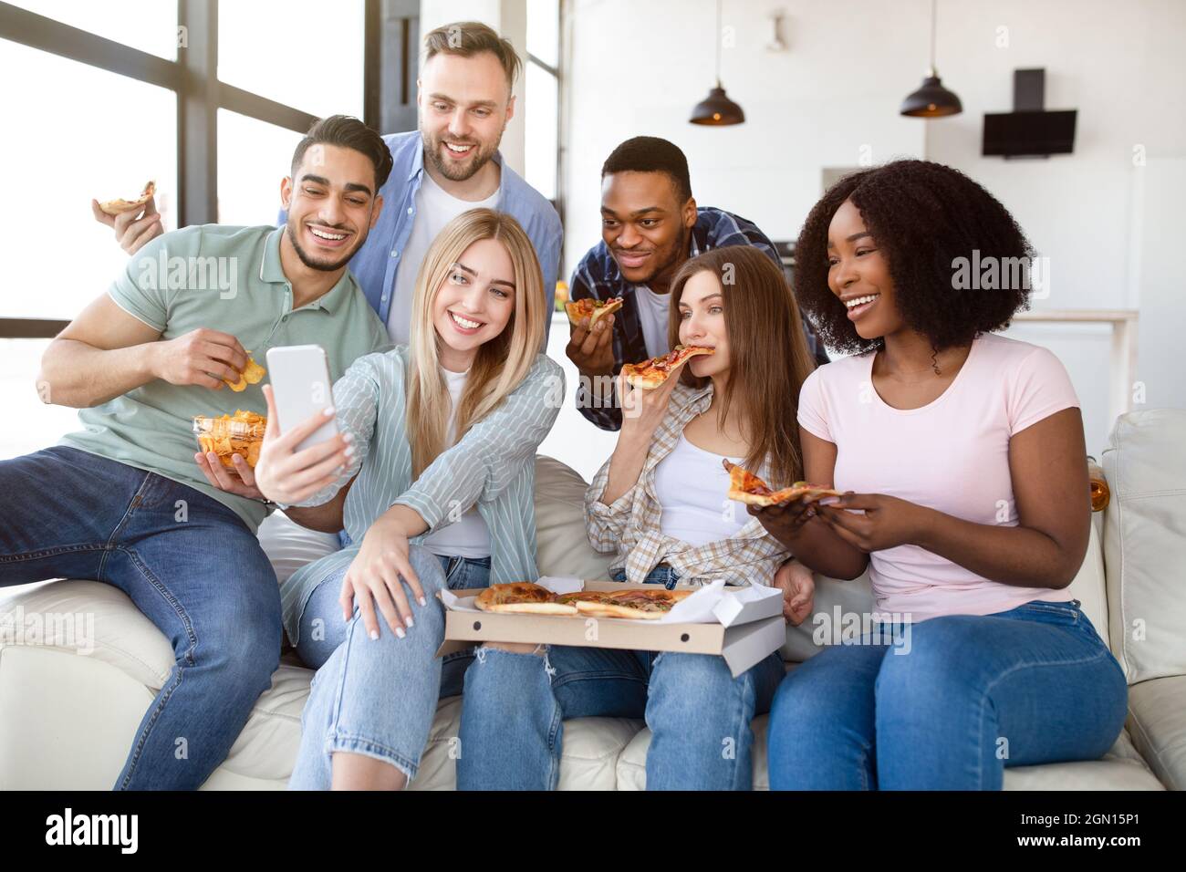 Happy diverse friends having party, sitting on sofa with pizza, chips ...
