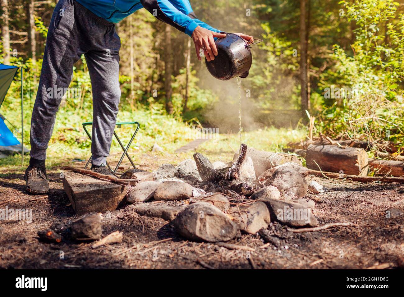 Man extinguishing campfire with water from cauldron in summer forest ...