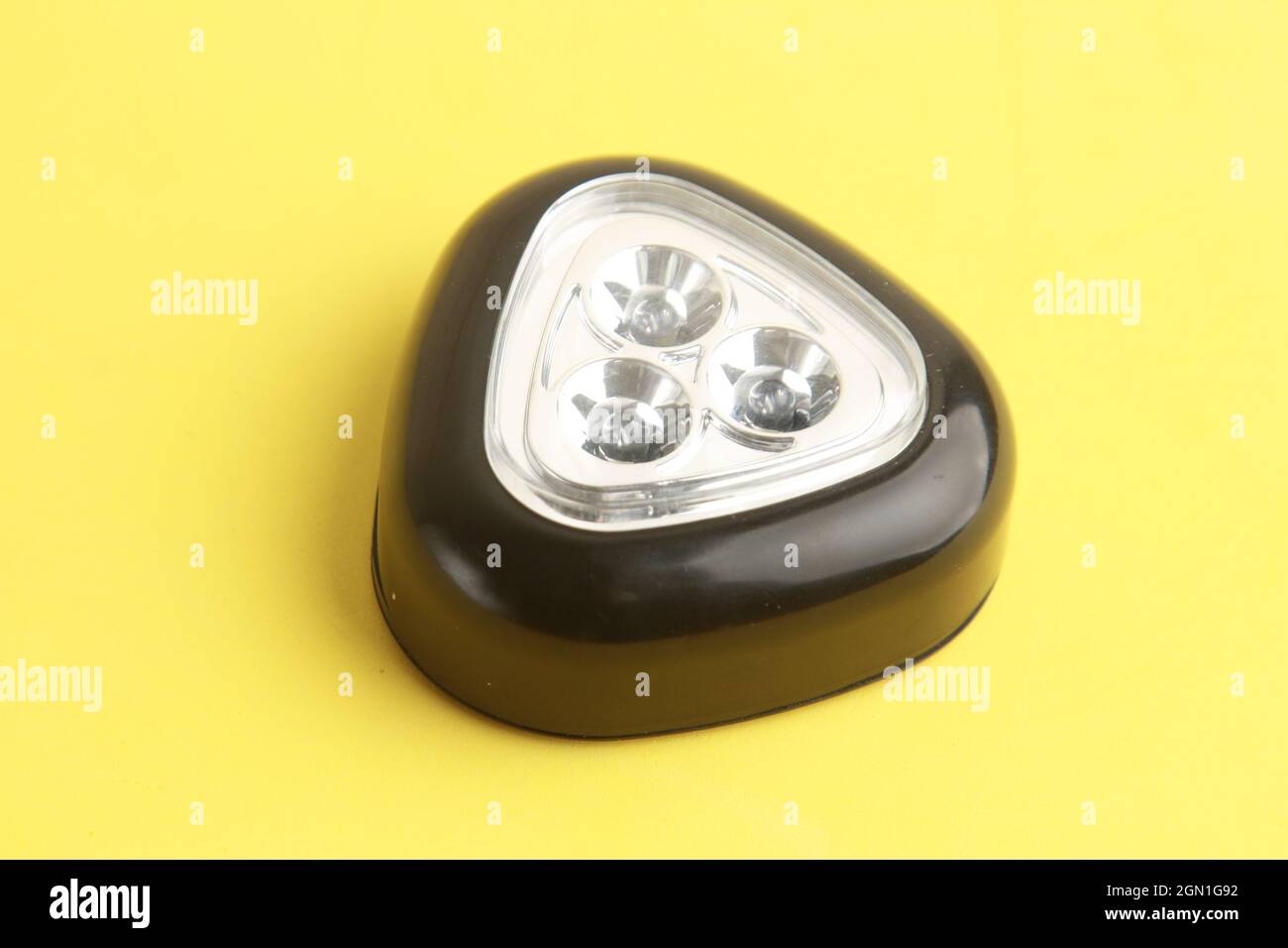 Closeup shot of a triangular black flashlight led light on a yellow background Stock Photo - Alamy
