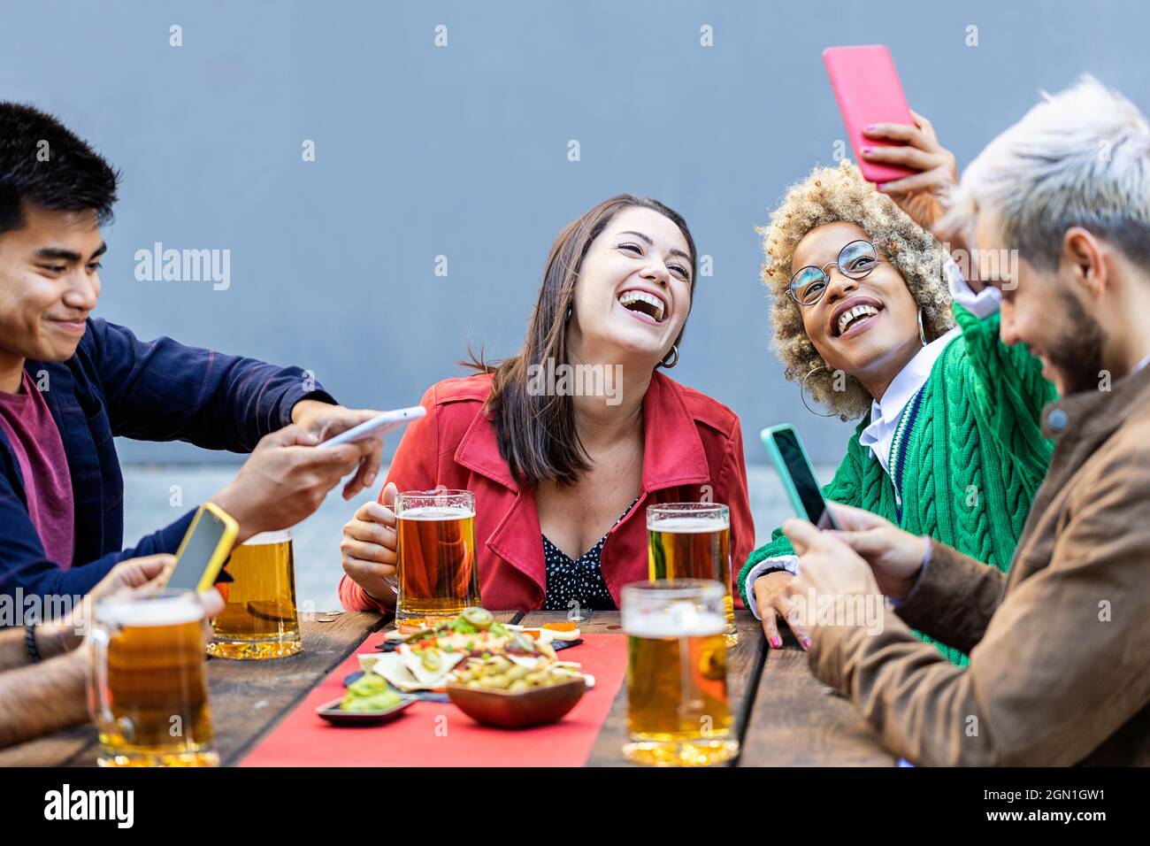 Group of happy millennial people using smartphone while drinking beer ...