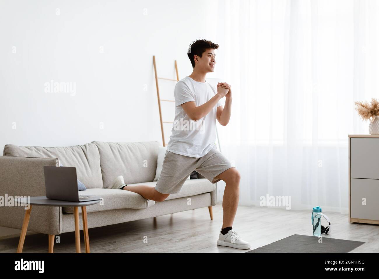 Asian guy doing split squats in front of laptop Stock Photo - Alamy