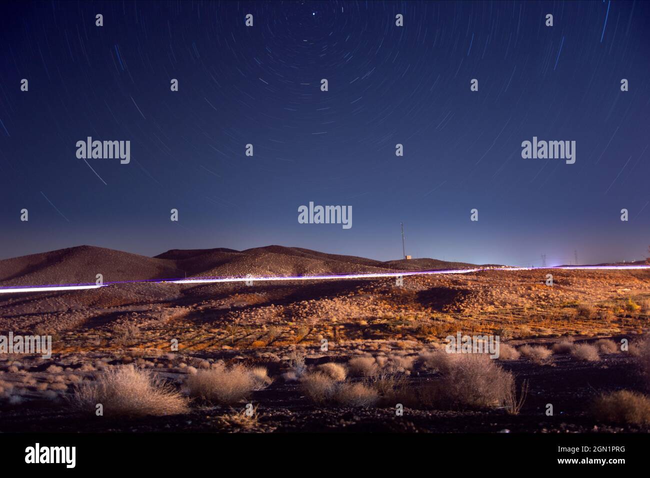 night view from plants and hills in desert with light and star trails ...