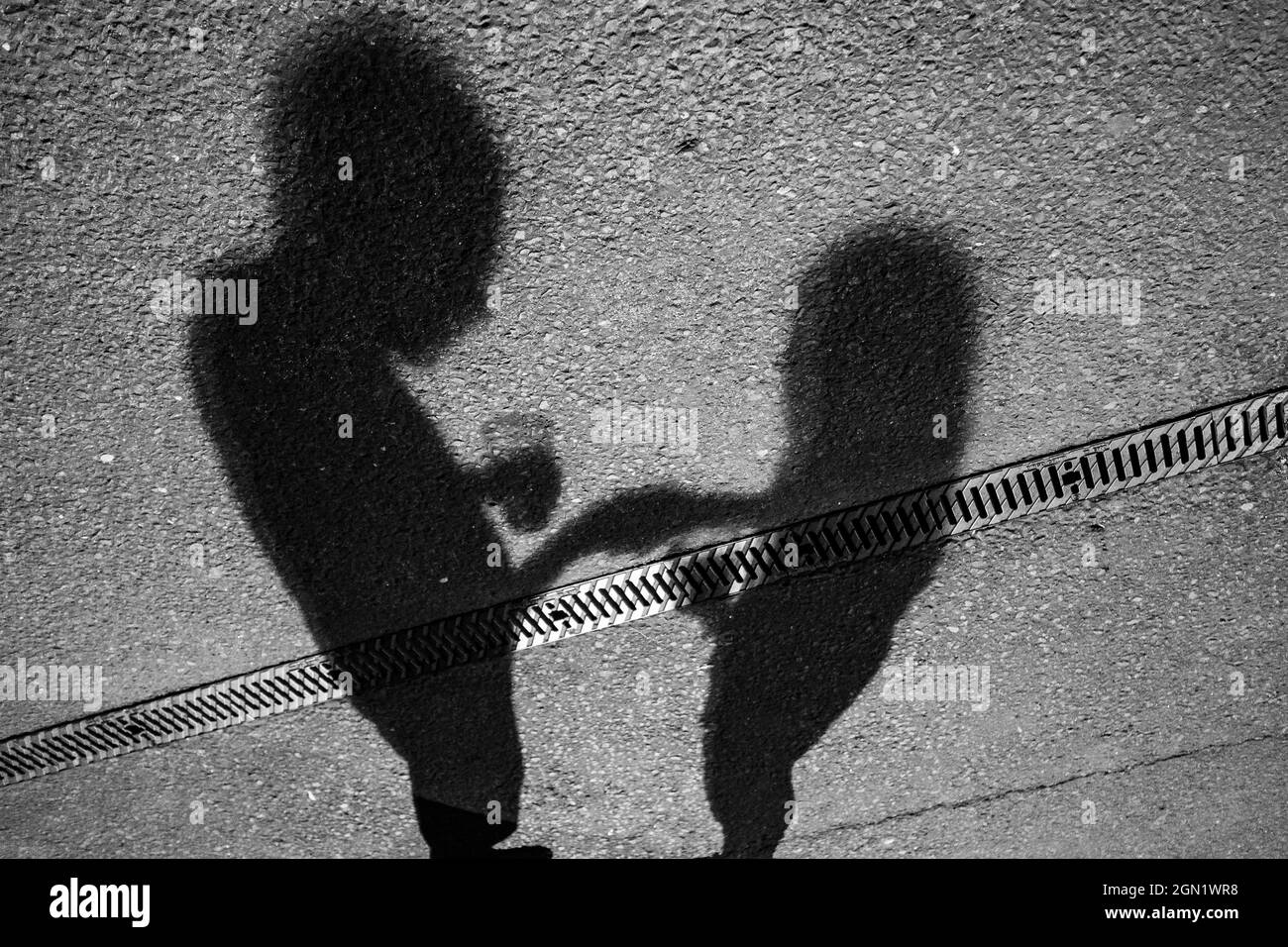 Shadows of a couple shaking hands and holding cups on an asphalt groun ...