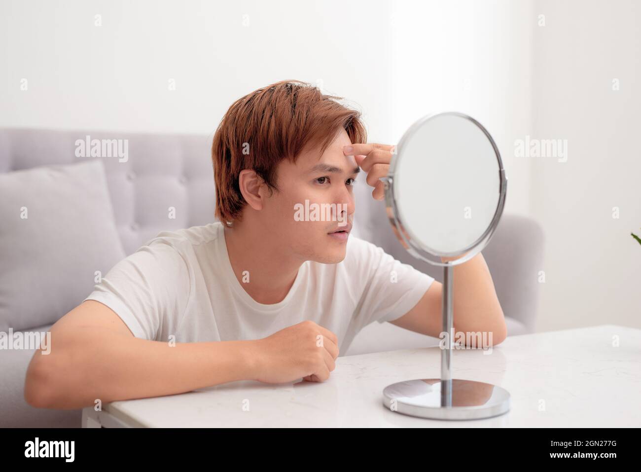 young handsome Asian man looking at his face in the mirror isolated ...