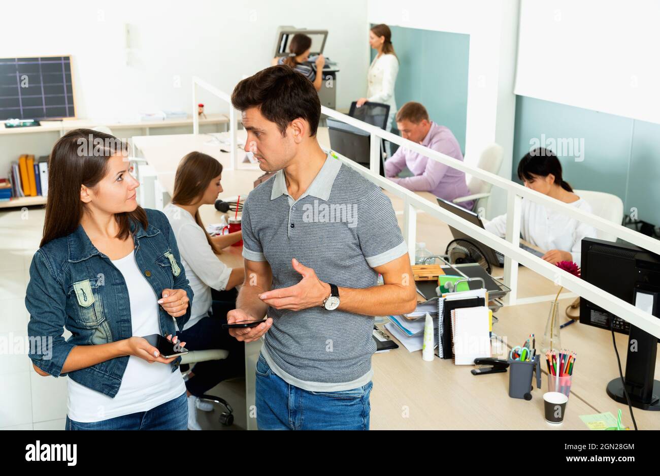 Friendly male and female colleagues exchanging phone numbers in modern ...