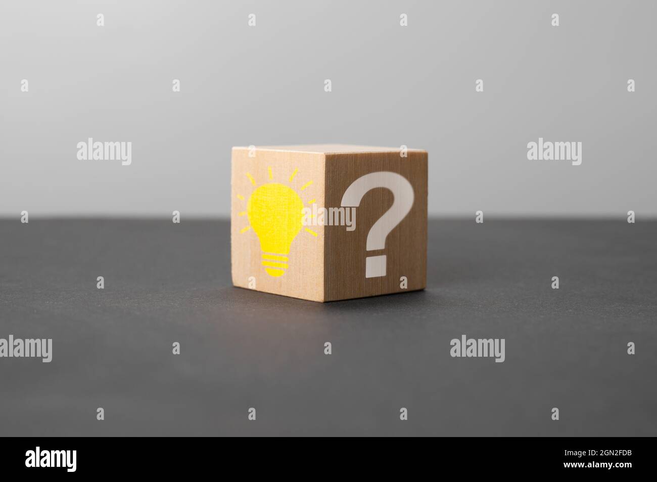 Wooden cube with bright light bulb and question mark on black table ...