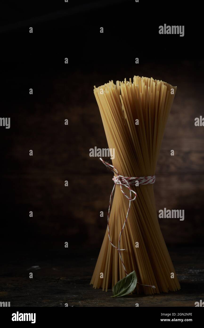 Bunch of dried spaghetti and green basil leaf served on table on black ...