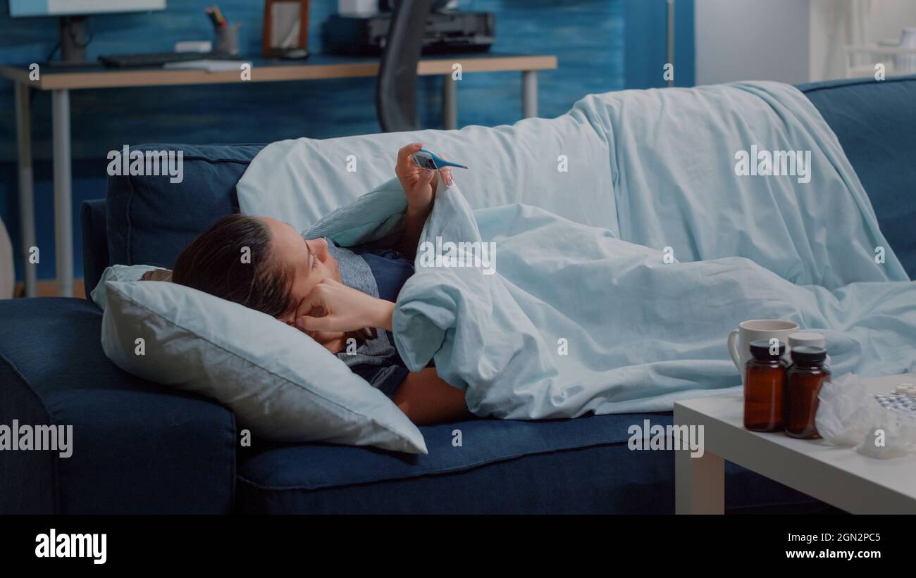 Ill person laying on couch and holding thermometer to check temperature ...