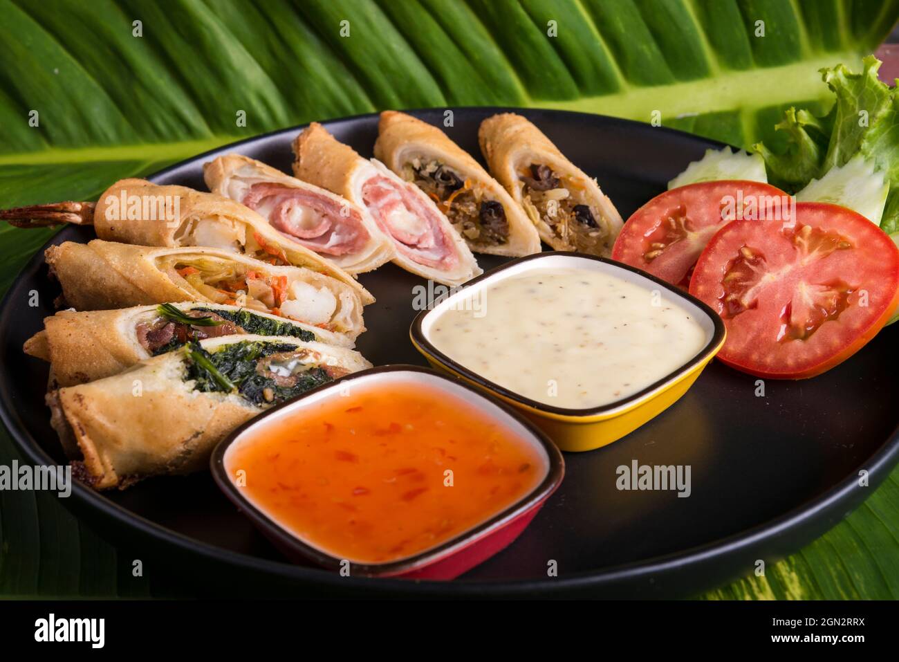 black plate with a fusion of spring rolls dispalyed with dipping sweet ...