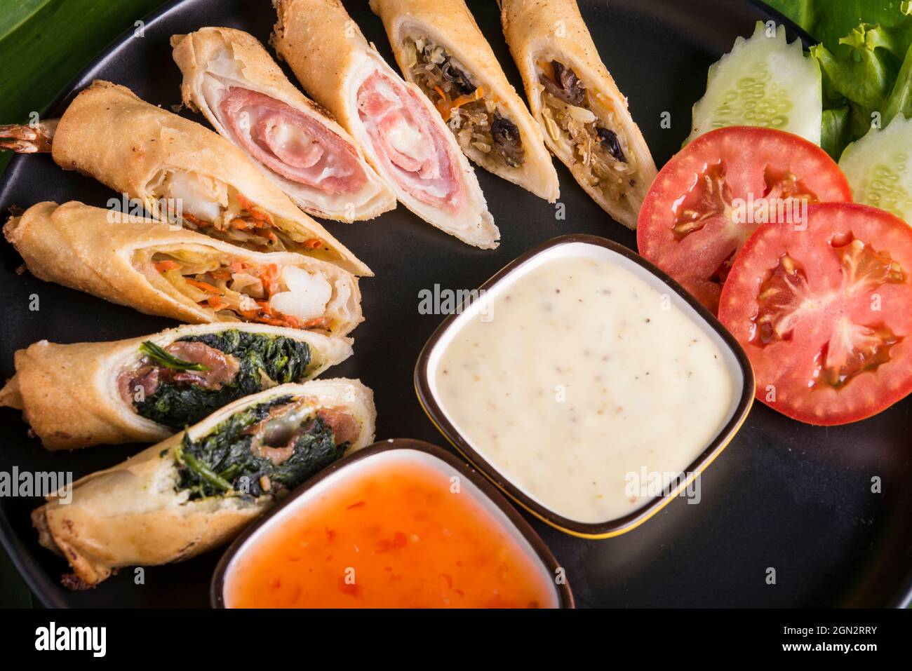 black plate with a fusion of spring rolls dispalyed with dipping sweet ...
