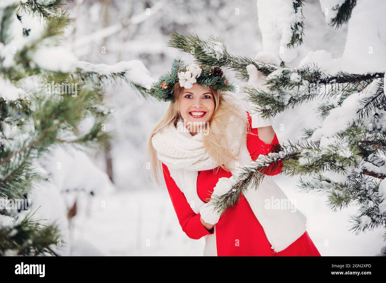 Portrait of a woman in a red jacket in a cold winter forest. Girl with a wreath on her head in a ...