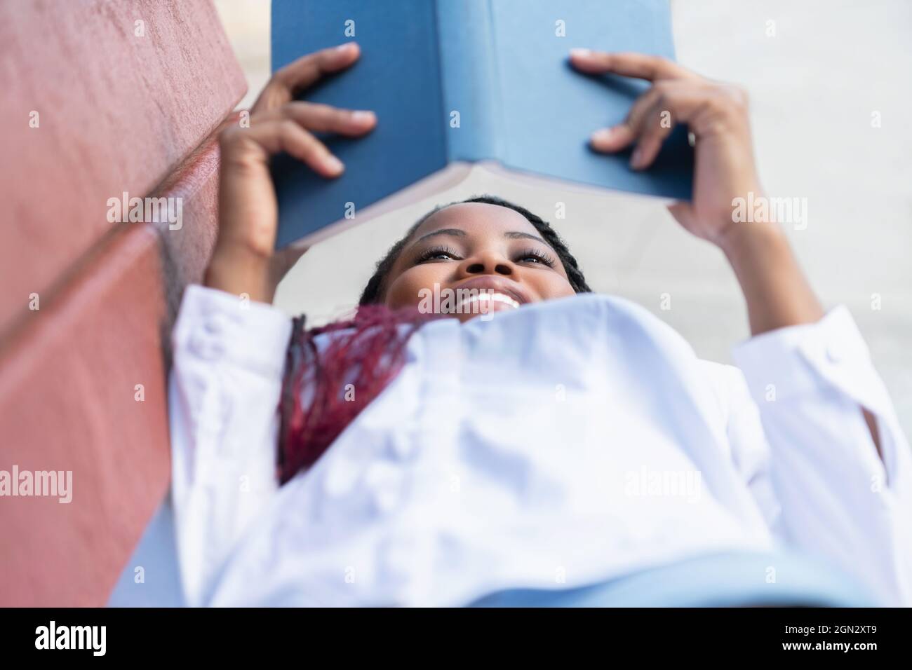 Smile face of an African woman reading a book while leaning in a ...