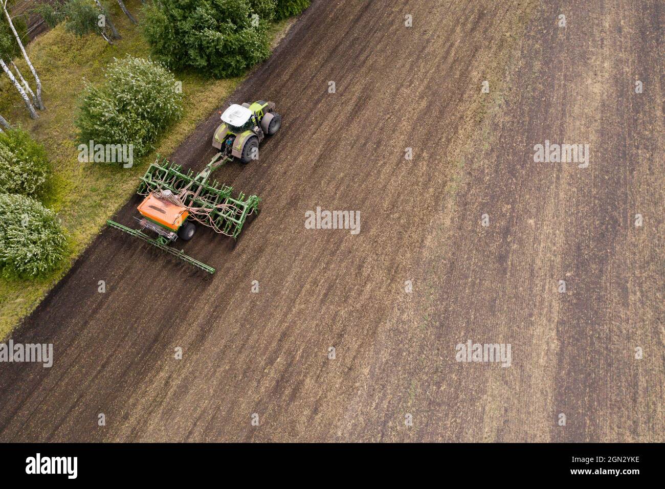 Aerial view of agricultural tractor with seeder machine at work on the ...