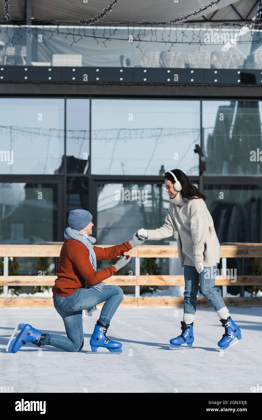 full length of young man holding box with ring and kneeling while ...