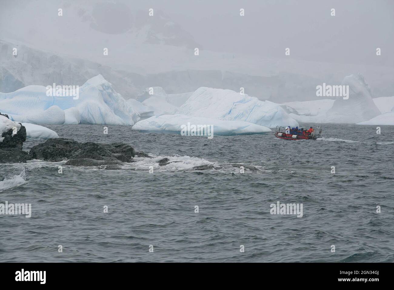 Boat sailing on the frosty waters in Antarctica with icebergs sticking ...