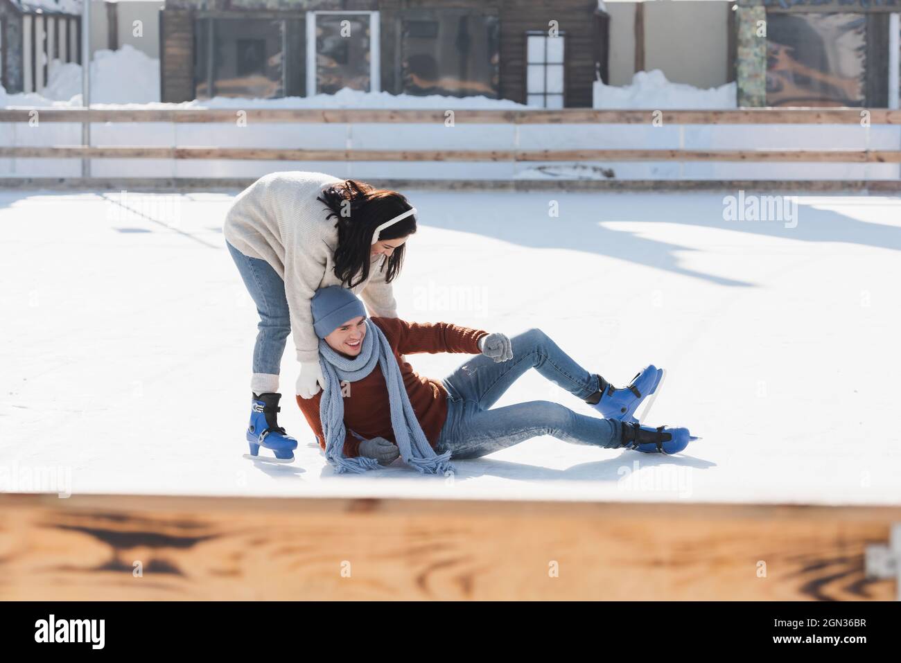 full length of happy man falling near woman while skating on ice rink ...