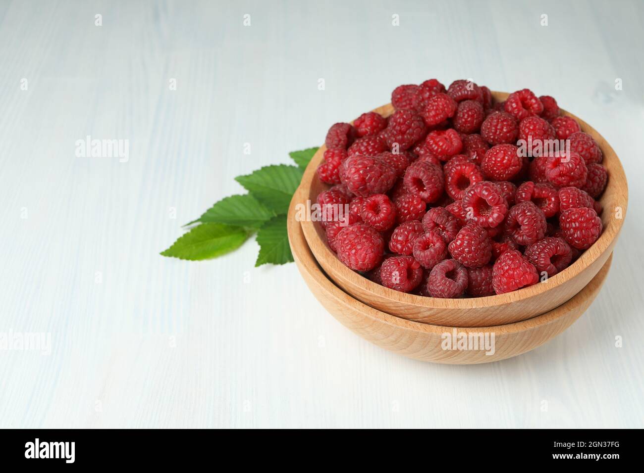 Red juicy raspberries in a wooden bowl on a white wooden background ...