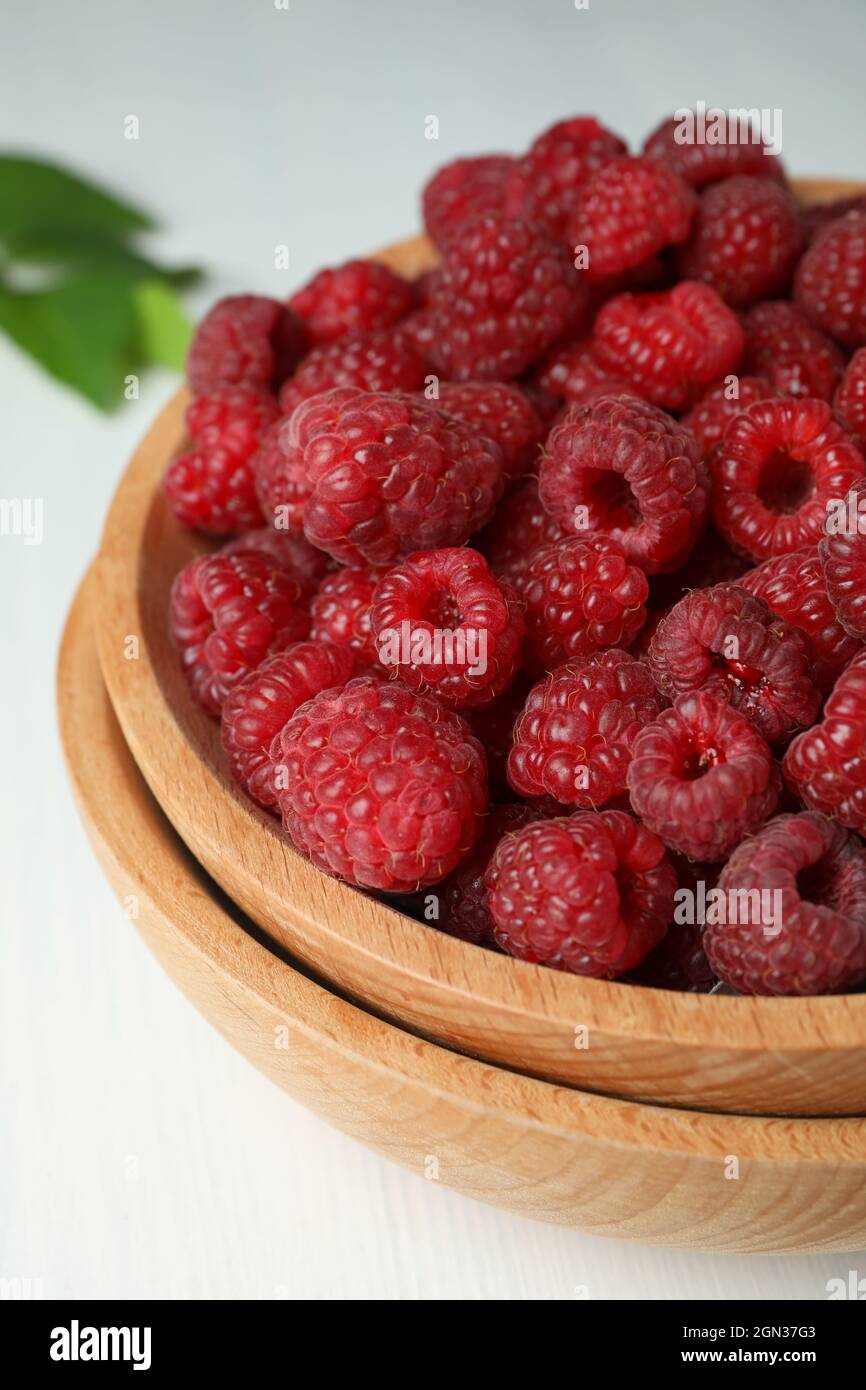 Red juicy raspberries in a wooden bowl on a white wooden background ...