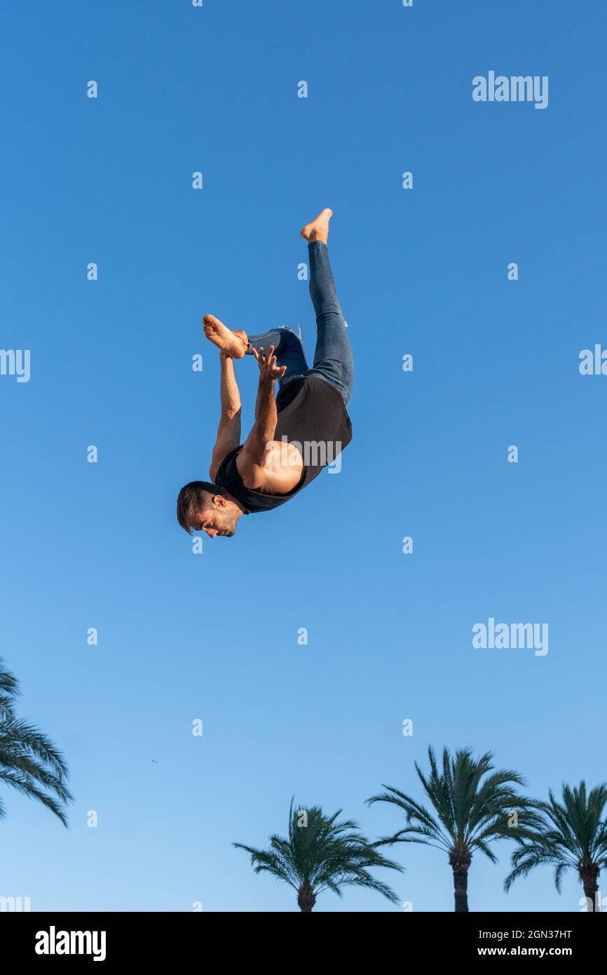 Low angle side view of active male athlete doing backbend while jumping ...