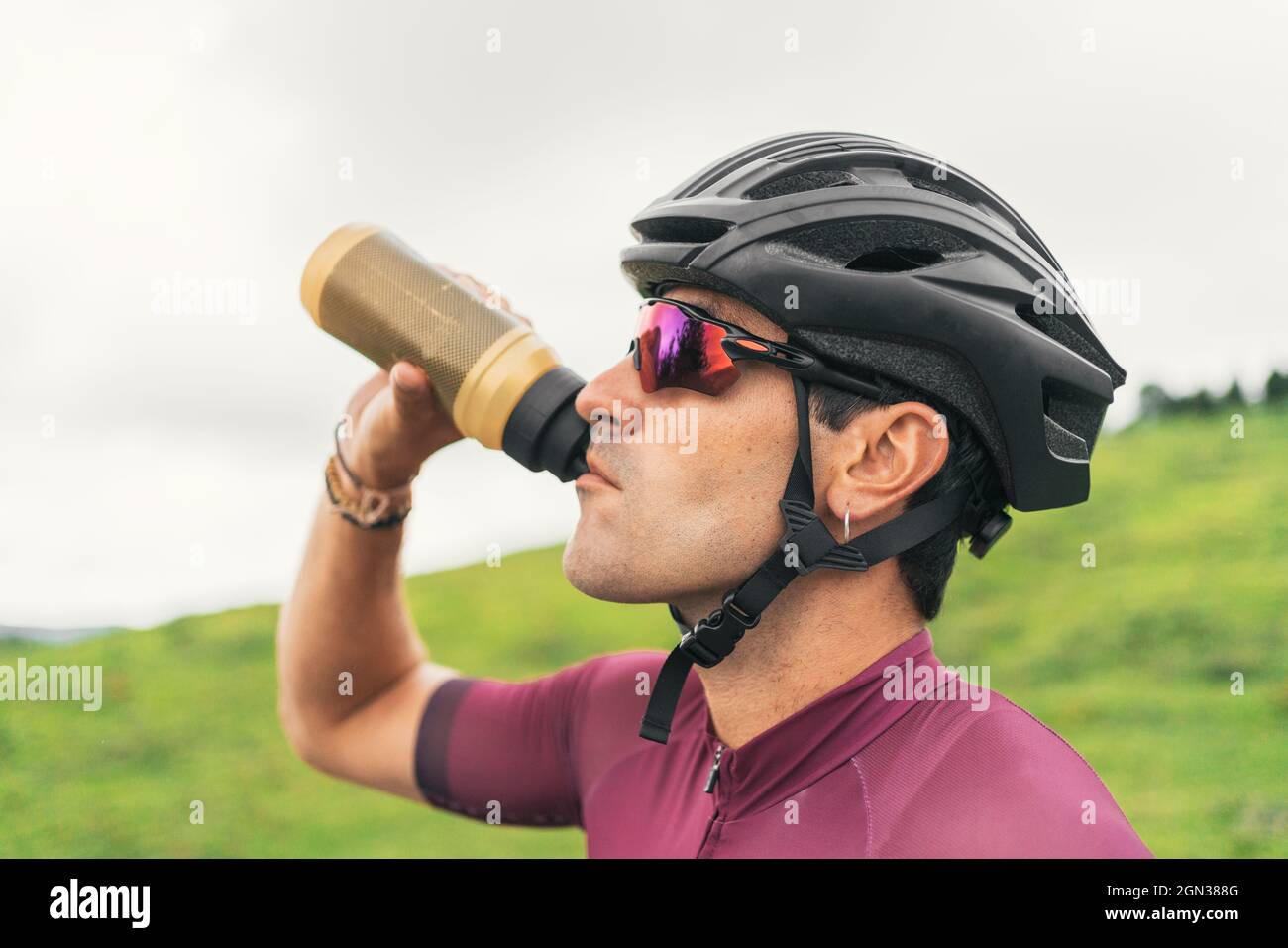 Side view of sportsman in cycling helmet and sunglasses drinking water ...