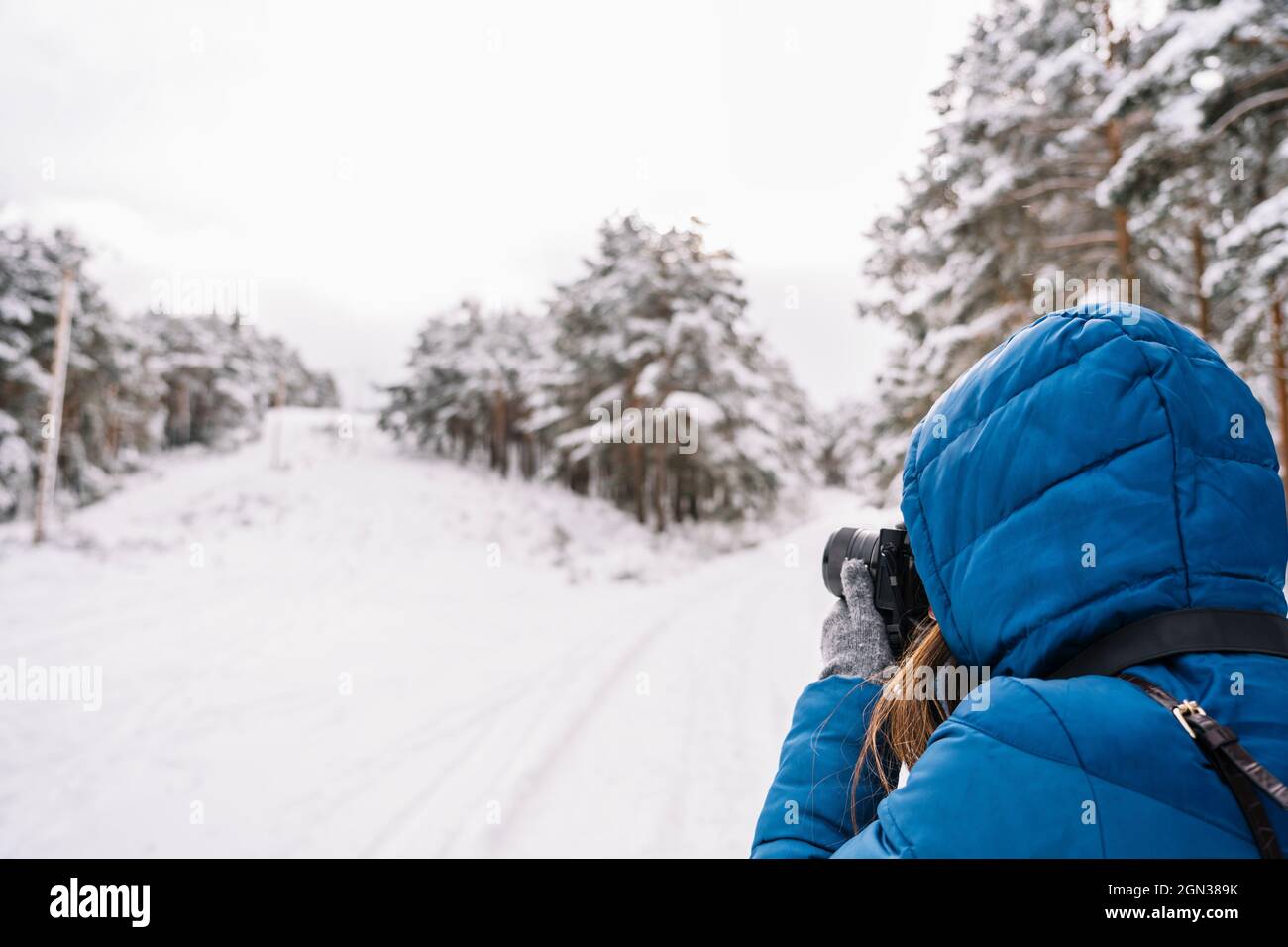 Young female in warm outerwear standing among snowy trees and taking ...