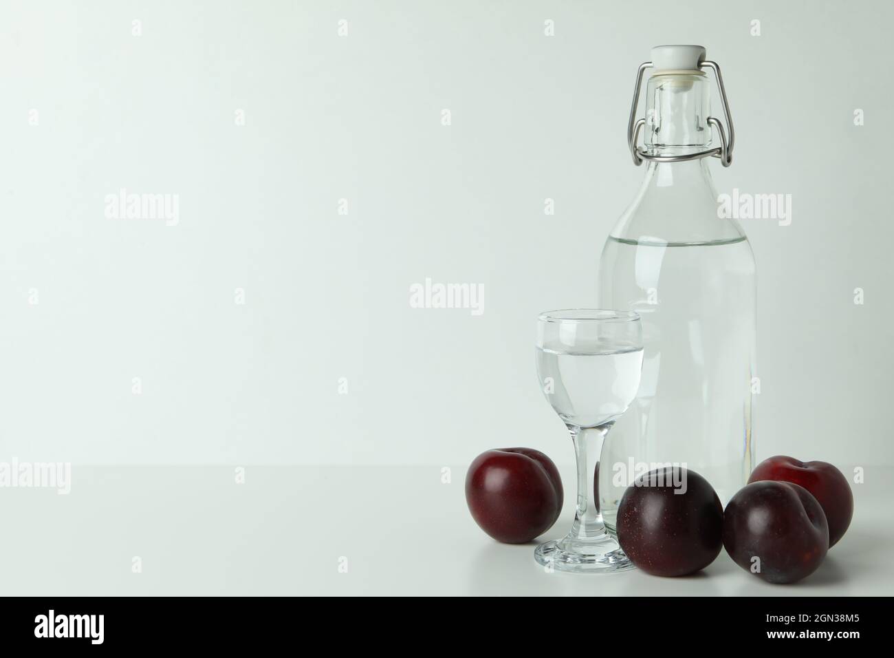 Bottle and shot of plum vodka and ingredients on white table Stock ...