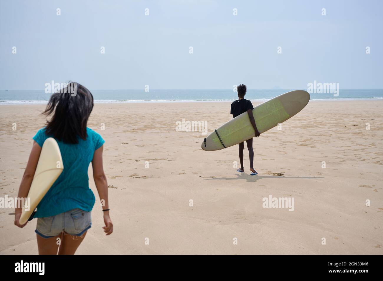 Back view of young multiethnic female surfers with surfboards speaking ...